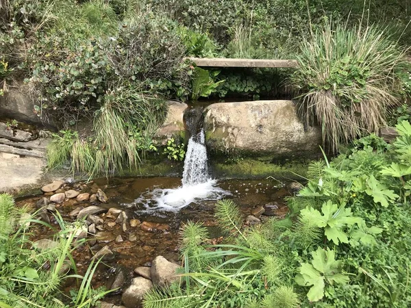 Small water fall flowing between two large rocks into a pool. - Stock ...