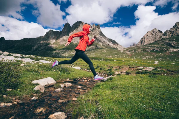 Woman trail runner jumping over samll river on beautiful mountains ...