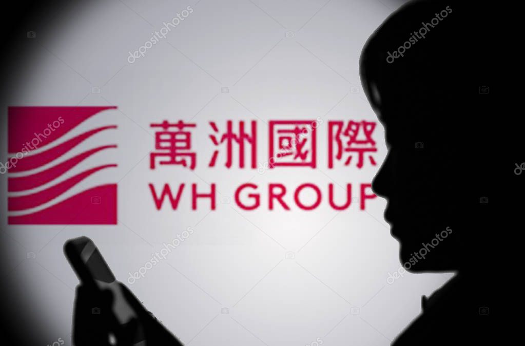 Un peatón usa su teléfono inteligente frente a un logotipo de WH Group ...