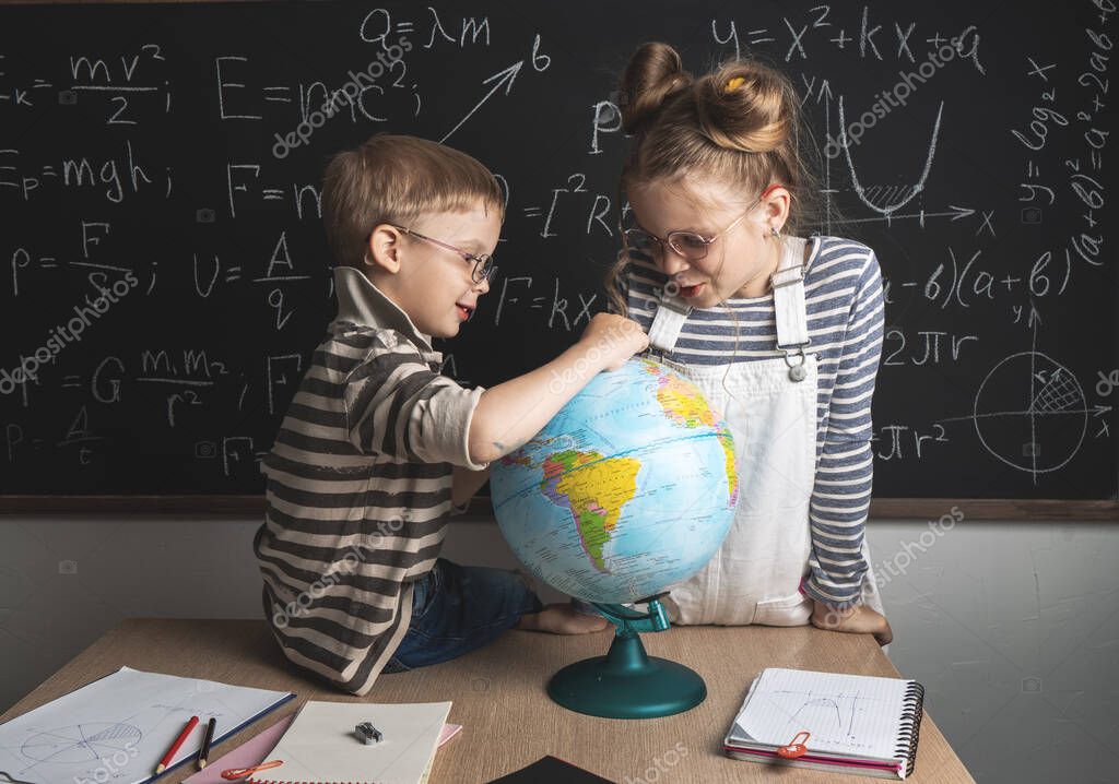 Lecci n de geograf a: Un ni o y una ni a est n sentados en un escritorio y estudiando el mundo ...