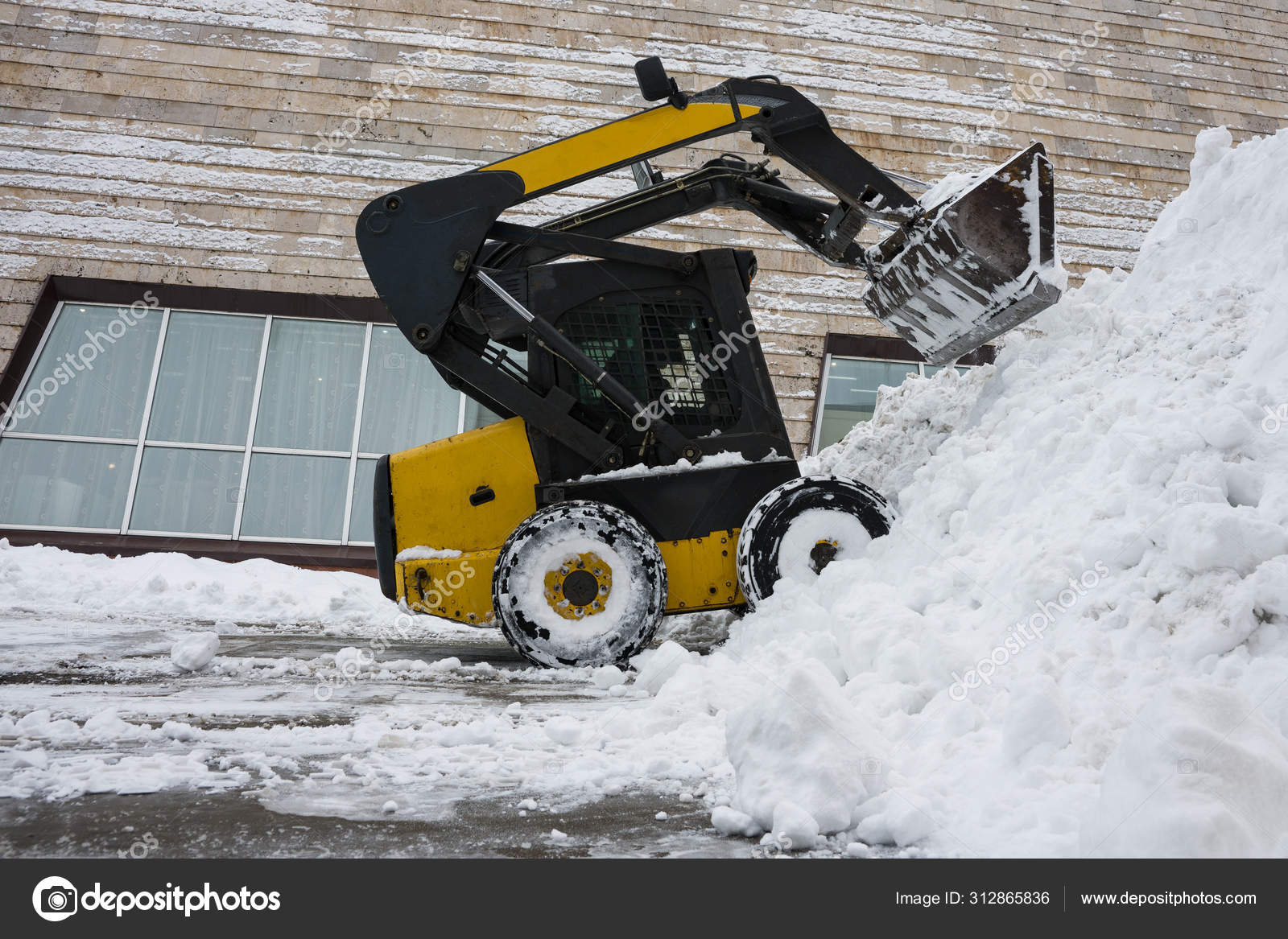 Minitractor shovels snow in a big pile. The background of the image is ...