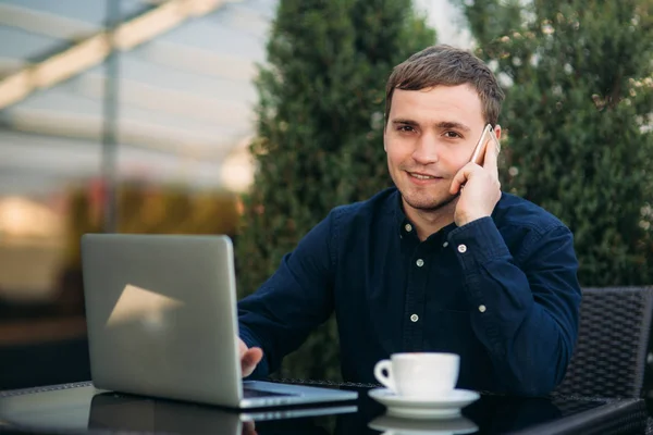 Young businessman call somebody and use laptop in cafe. Happy young man ...