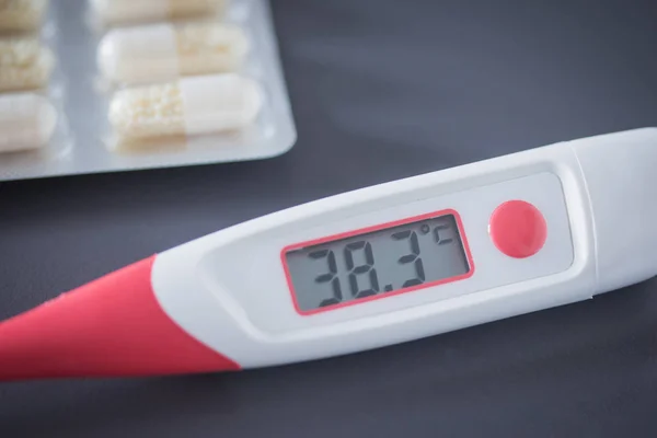 Red fever thermometer with digital display and pills lying on the desk ...