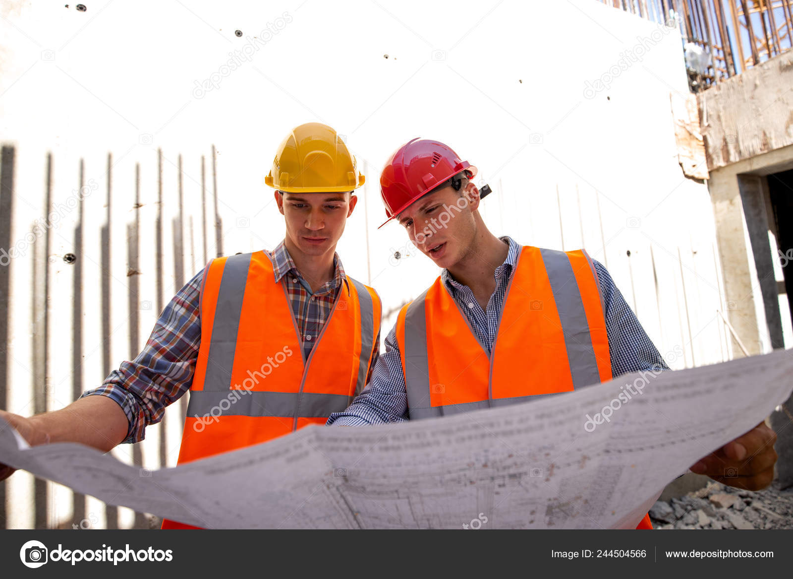Construction manager and engineer dressed in work clothes and hard hats ...