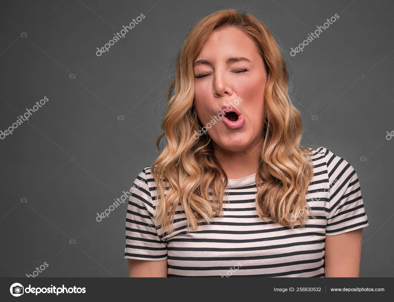 A young woman is squinting a sour grimace while standing against grey ...