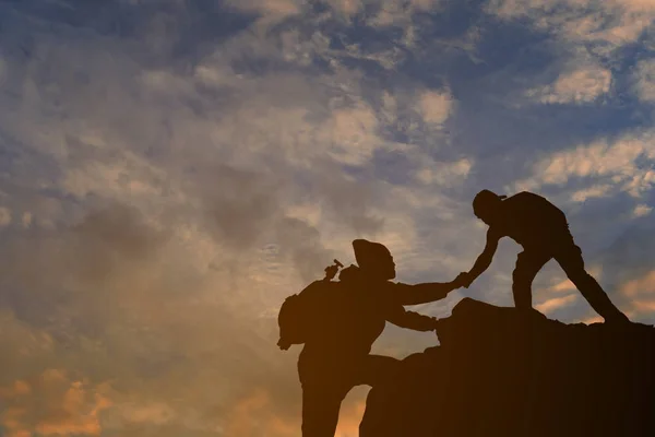 Two friends helping each other trying to reach top of mountains during ...