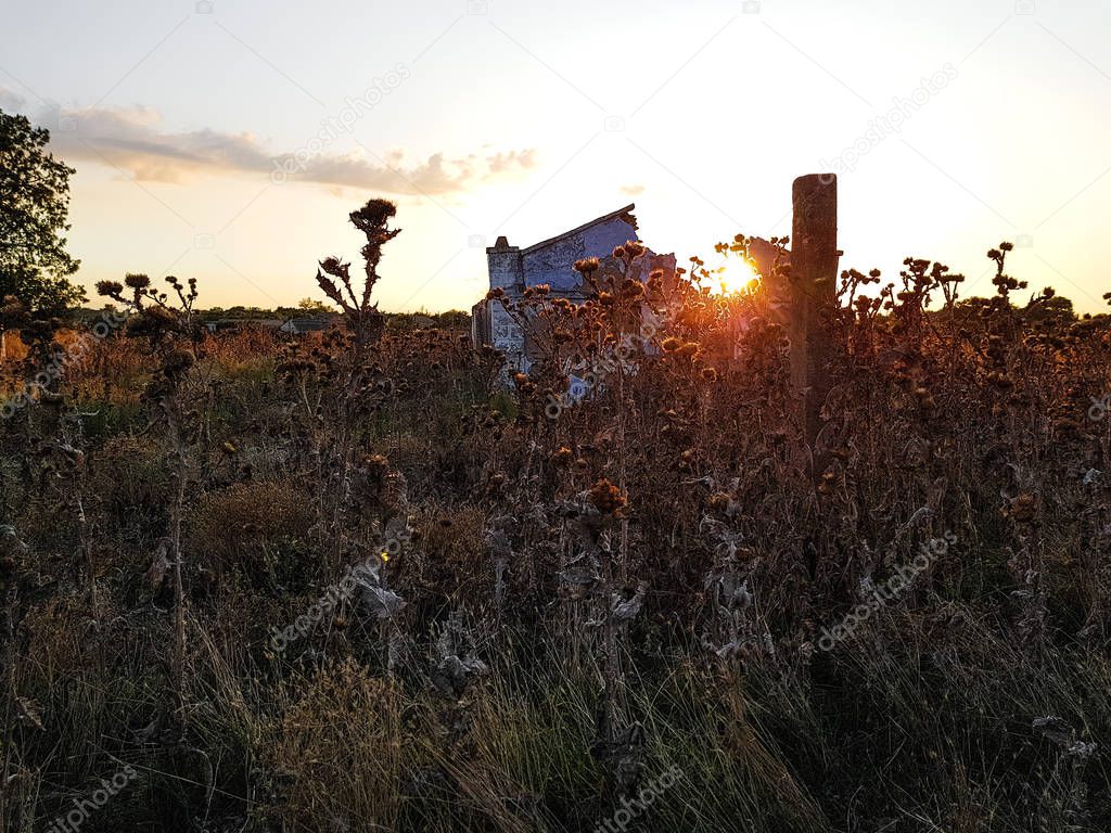 Arruinó una antigua casa rural sobre un fondo de atardecer. Los rayos del sol poniente brillan a ...