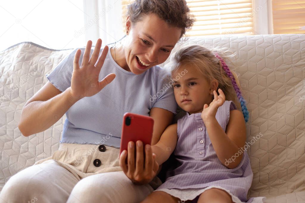 Feliz joven madre con su hija pequeña haciendo videollamadas con smartphone, haciendo un gesto ...