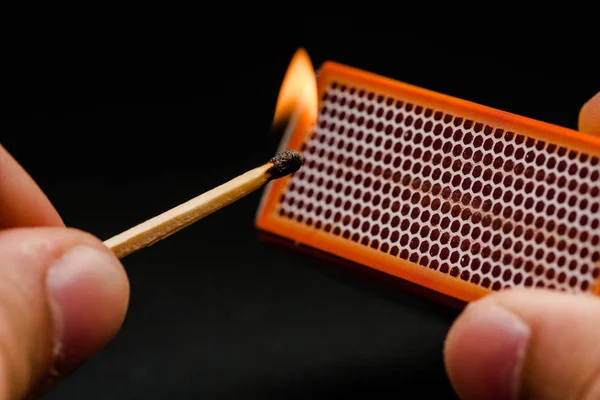 Man's fingers lighting a match, setting fire on friction. On a black ...