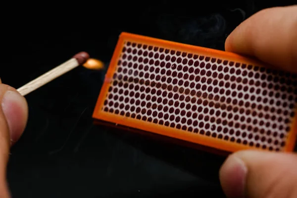 Man's fingers lighting a match, setting fire on friction. On a black ...