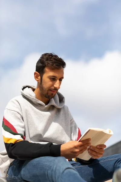 Young Bearded Man Reading A Book Sitting In A Park During The Morning ...