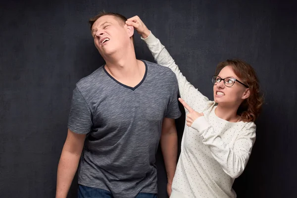 Enraged woman is pulling man by ear and scolding him - Stock Image ...