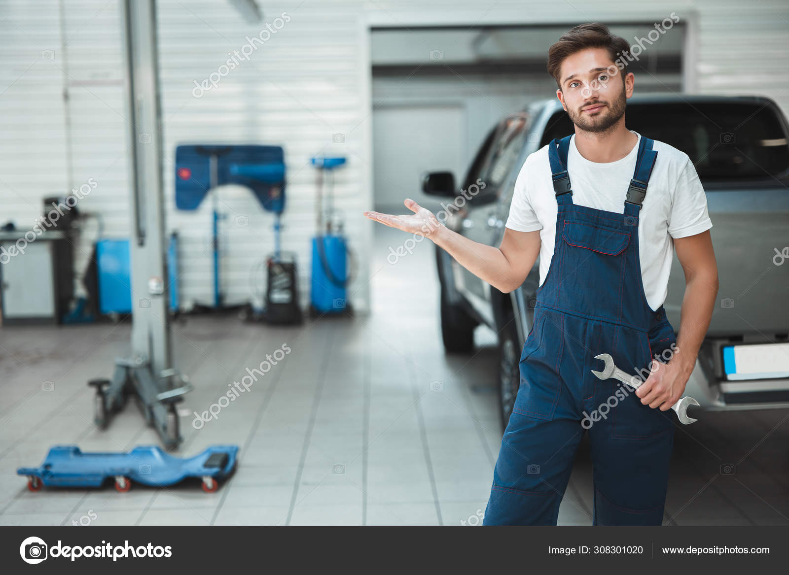 Young handsome mechanic wearing uniform with spanner in his hand ...