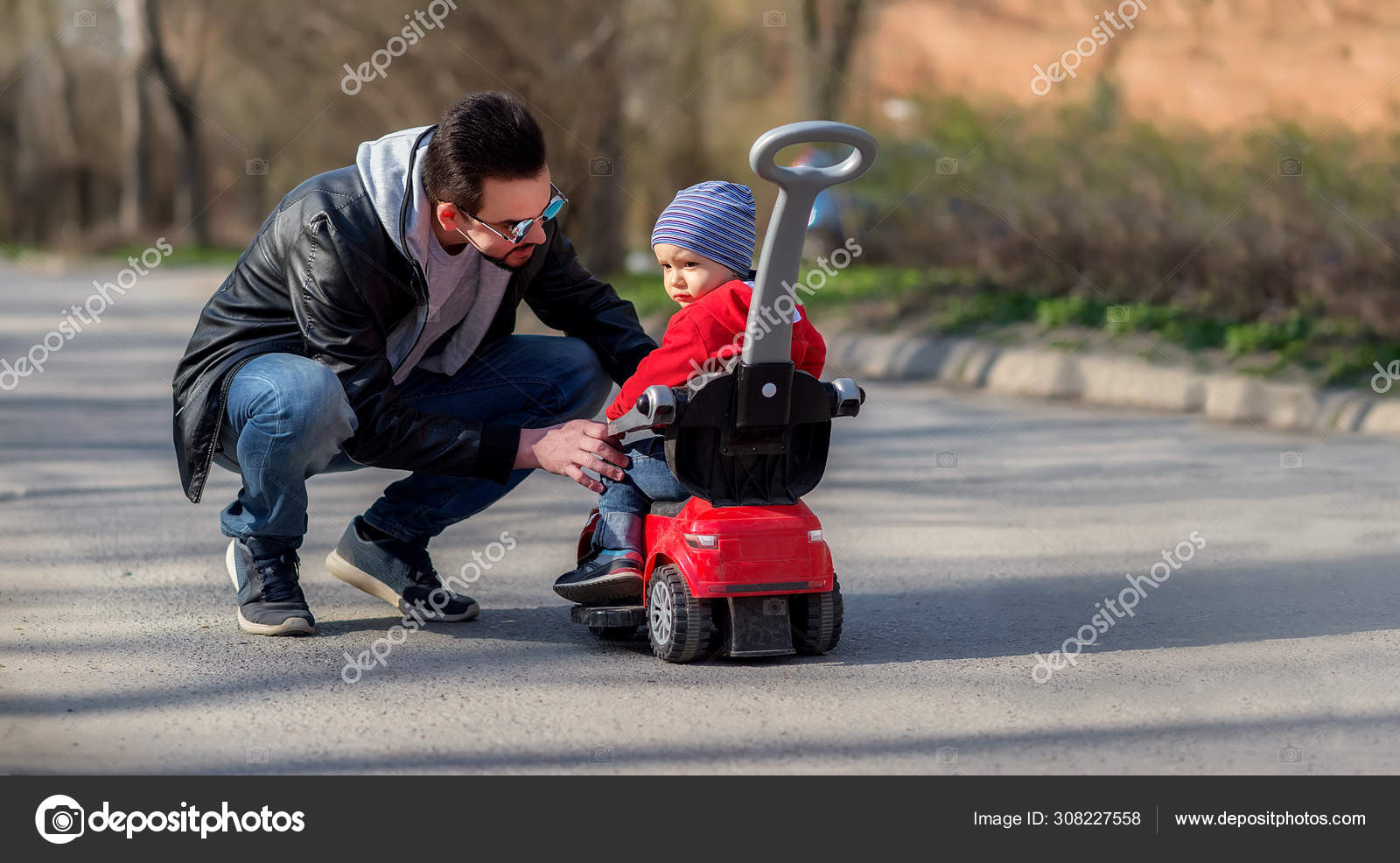 Little child is sitting on a red push car, his father is sitting ...