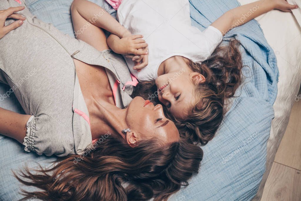 Feliz familia cariñosa tumbada relajante disfrutando en dormitorio juntos. Madre y su linda hija ...