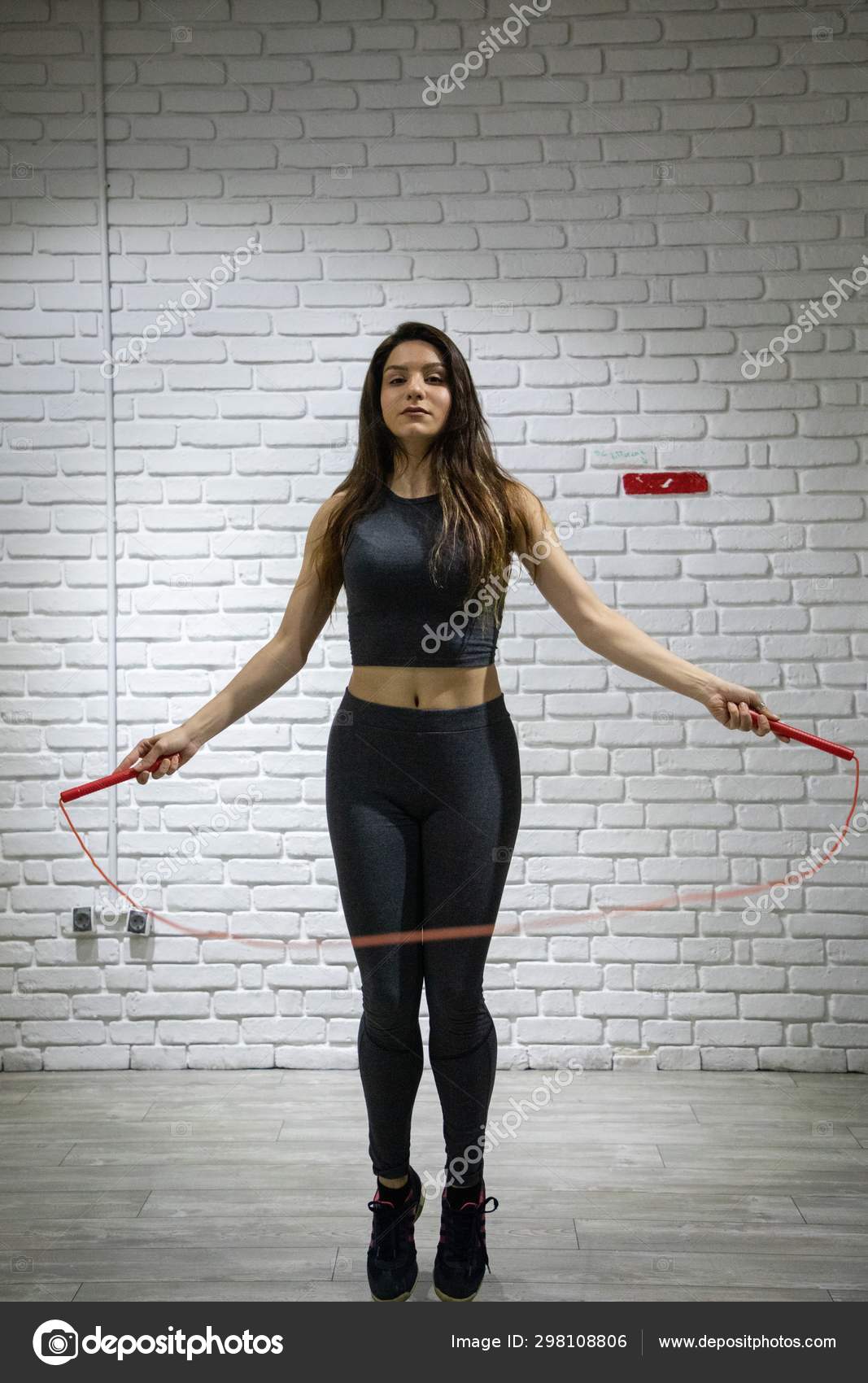 Attractive female model doing rope jumping in a yoga outfit in a white ...