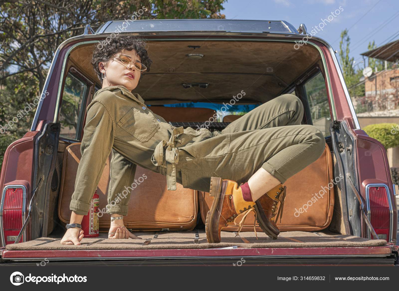 Curly stylish model posing for a photshot on the back of a car on a ...