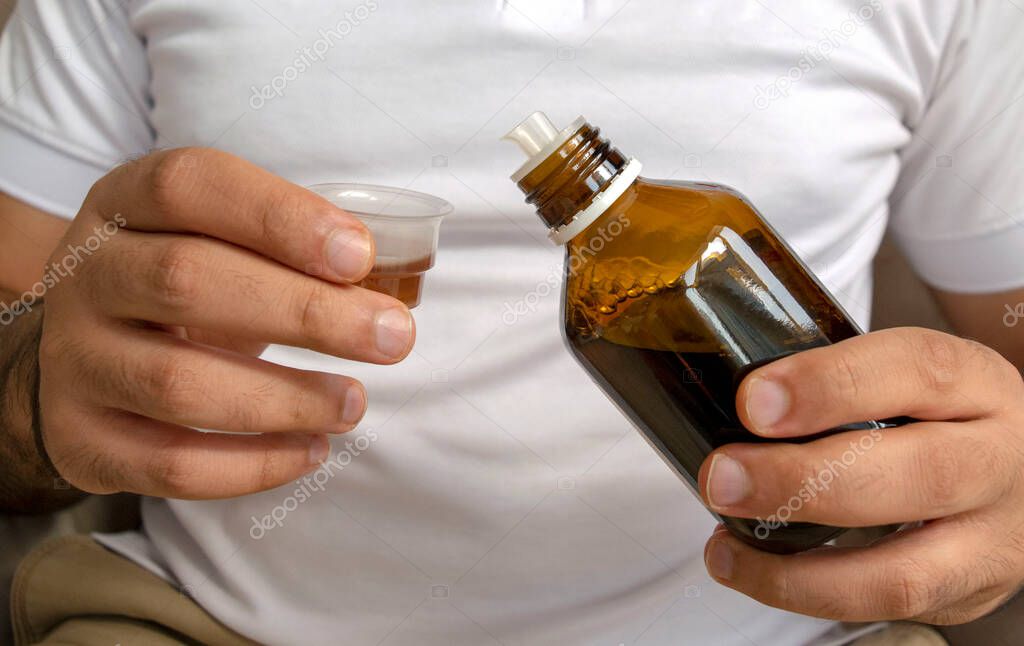 Hombre joven con camiseta blanca está vertiendo jarabe médico en la ...