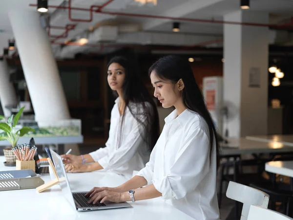 Portrait of two female office workers working with laptop on office ...