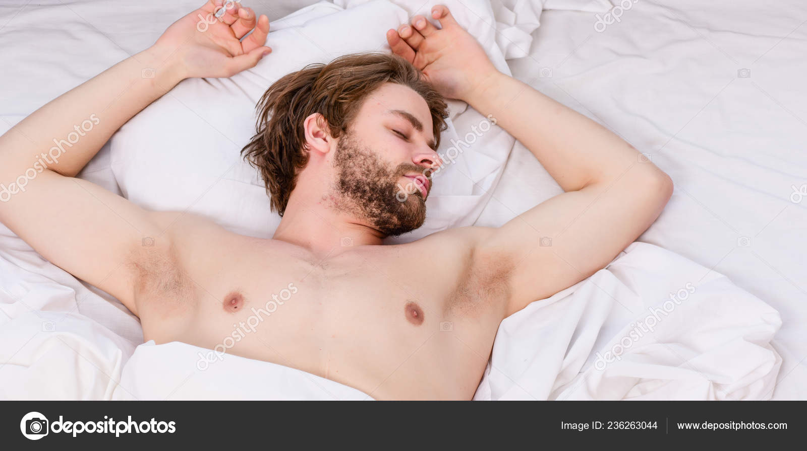 Picture showing young man stretching in bed. Young man stretching while waking up in the morning ...