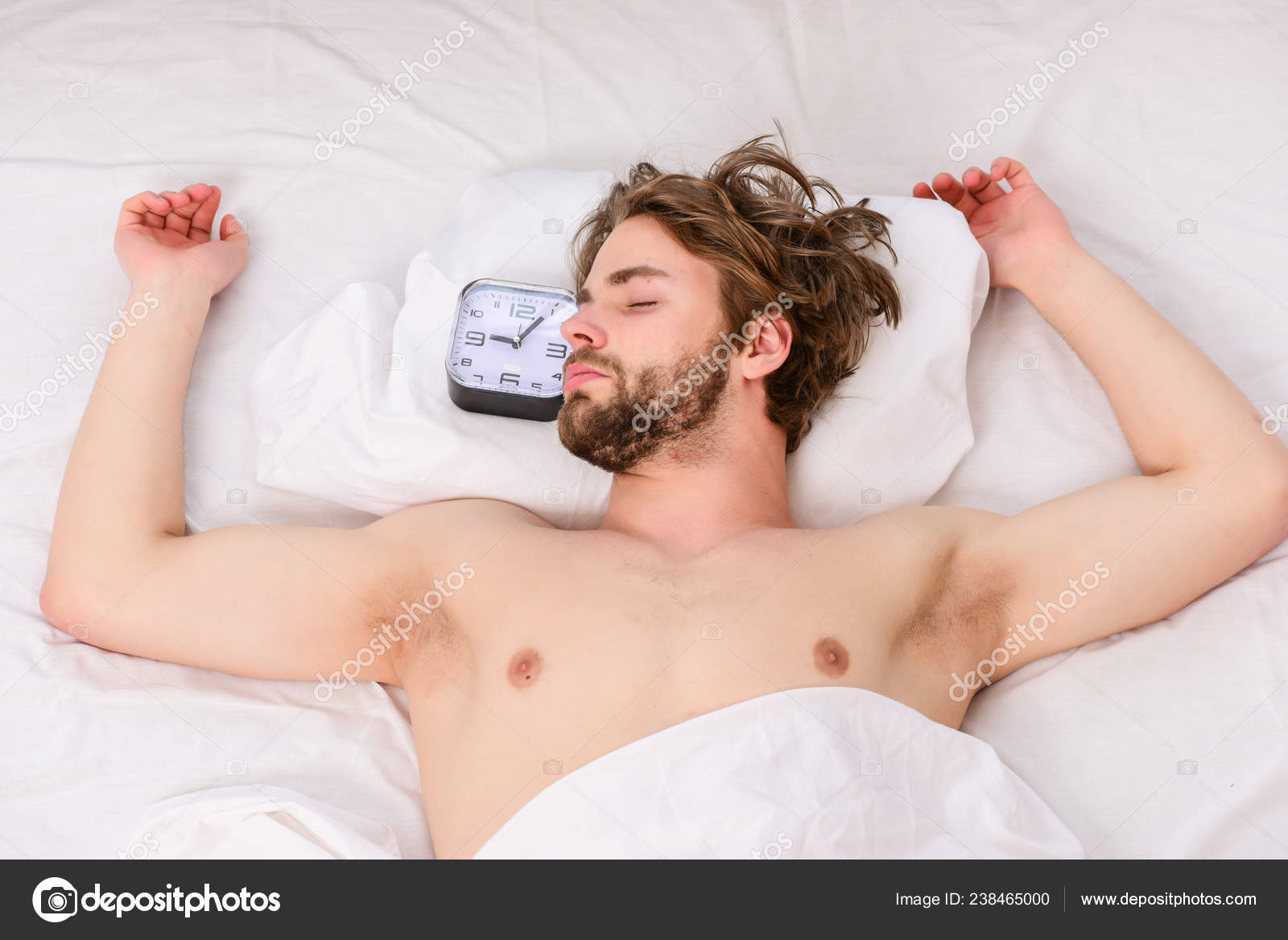 A young man waking up in bed and stretching his arms. Young man stretching while waking up in ...