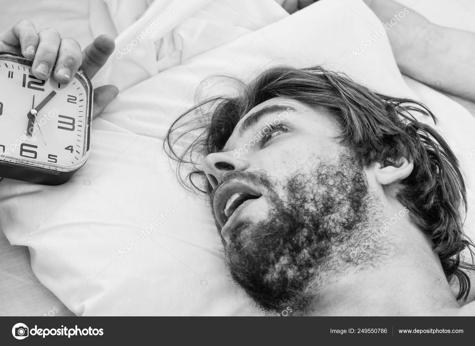 Handsome man using clock in bed after waking up in the morning. Lazy ...