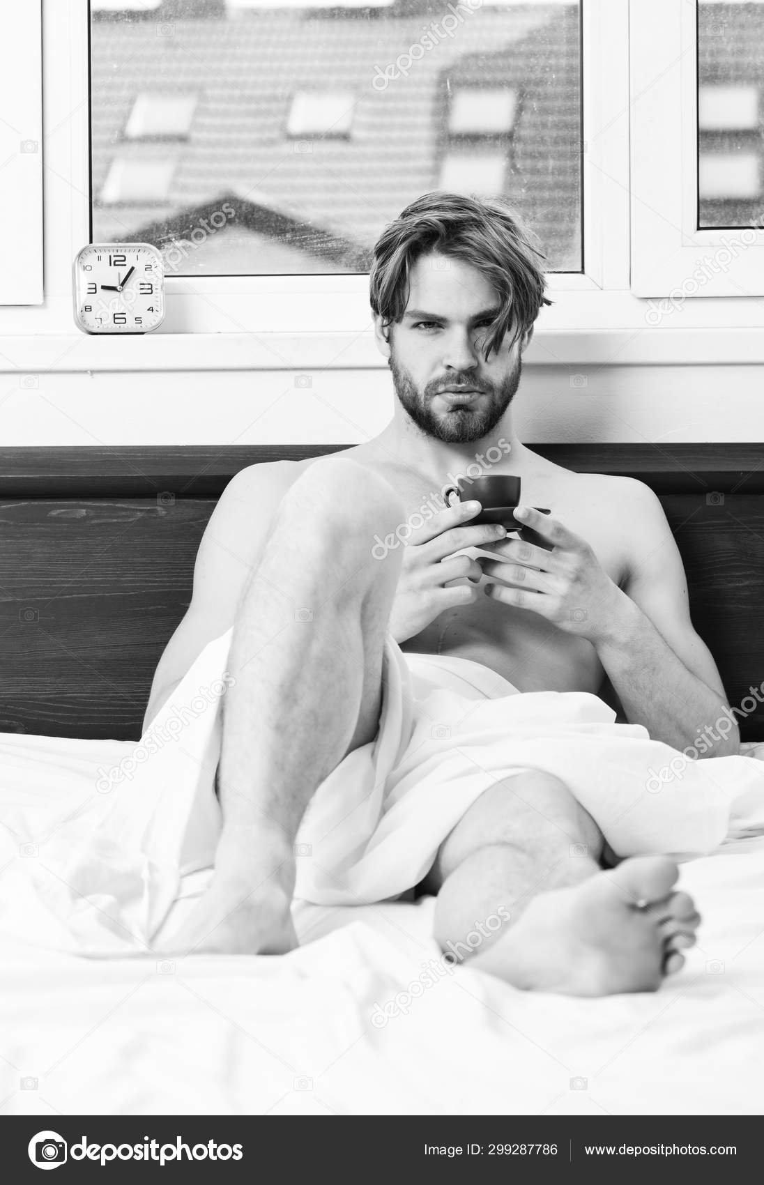 A young man waking up in bed and stretching his arms. Feet of man sleeping in comfortable bed ...