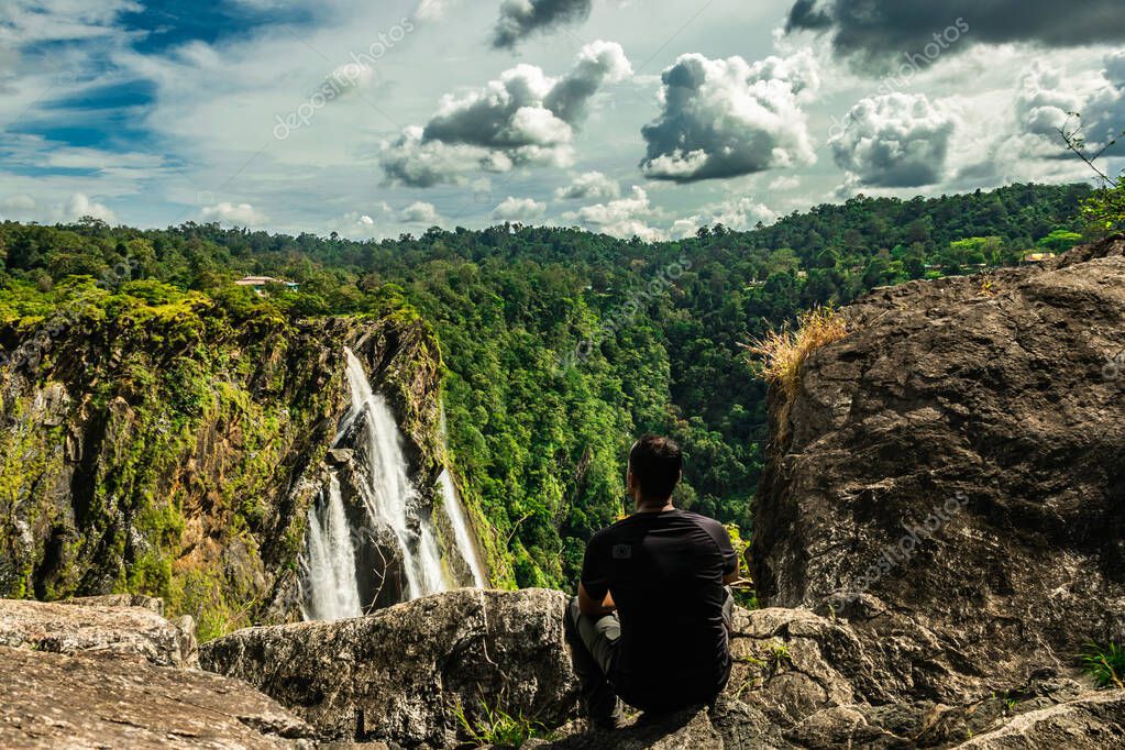 hombre sentado en la cima de la colina viendo la hermosa cascada en la ...