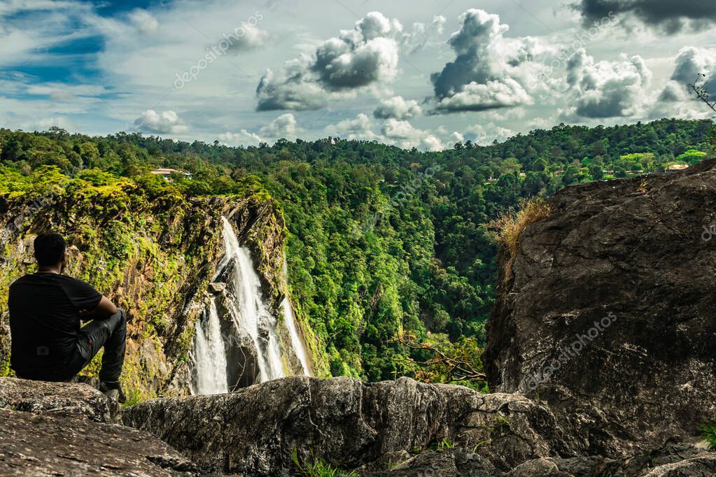 hombre sentado en la cima de la colina viendo la hermosa cascada en la ...