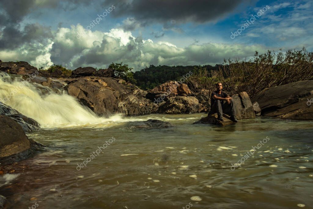 hombre sentado en la roca observando la hermosa cascada en la imagen de ...