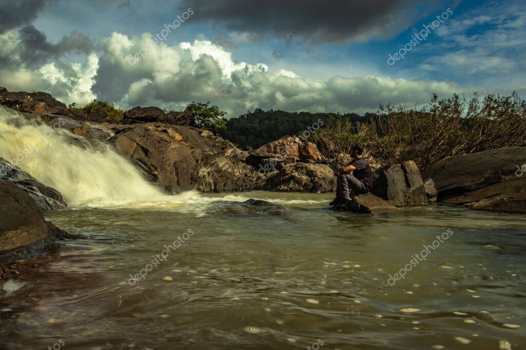 hombre sentado en la roca observando la hermosa cascada en la imagen de ...