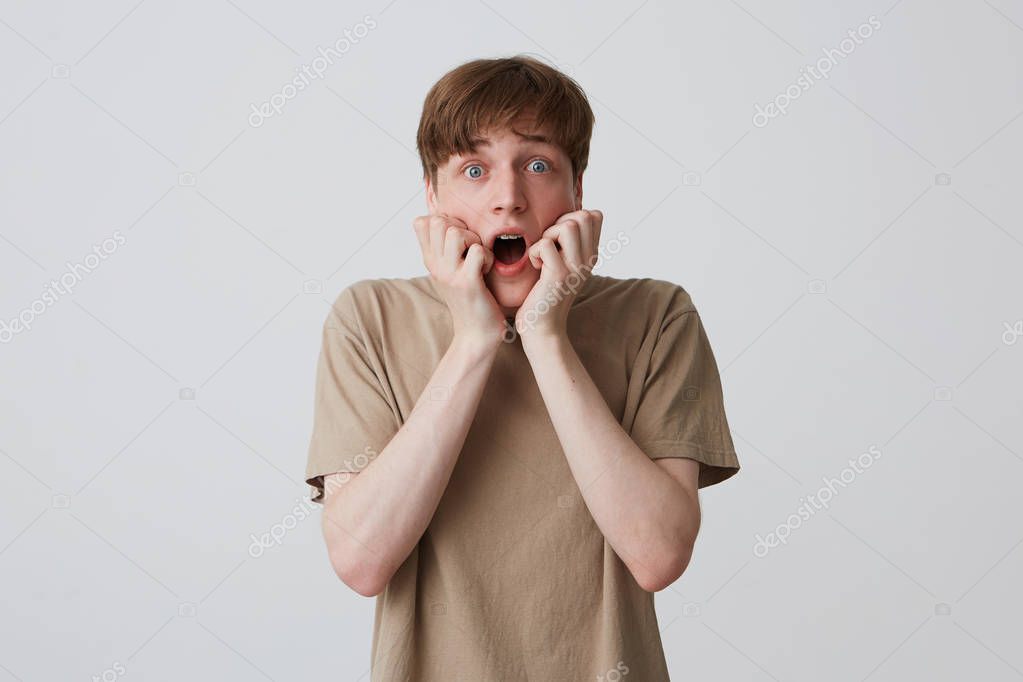 Primer plano del joven asustado en camiseta beige con corte de pelo corto y boca abierta parece ...