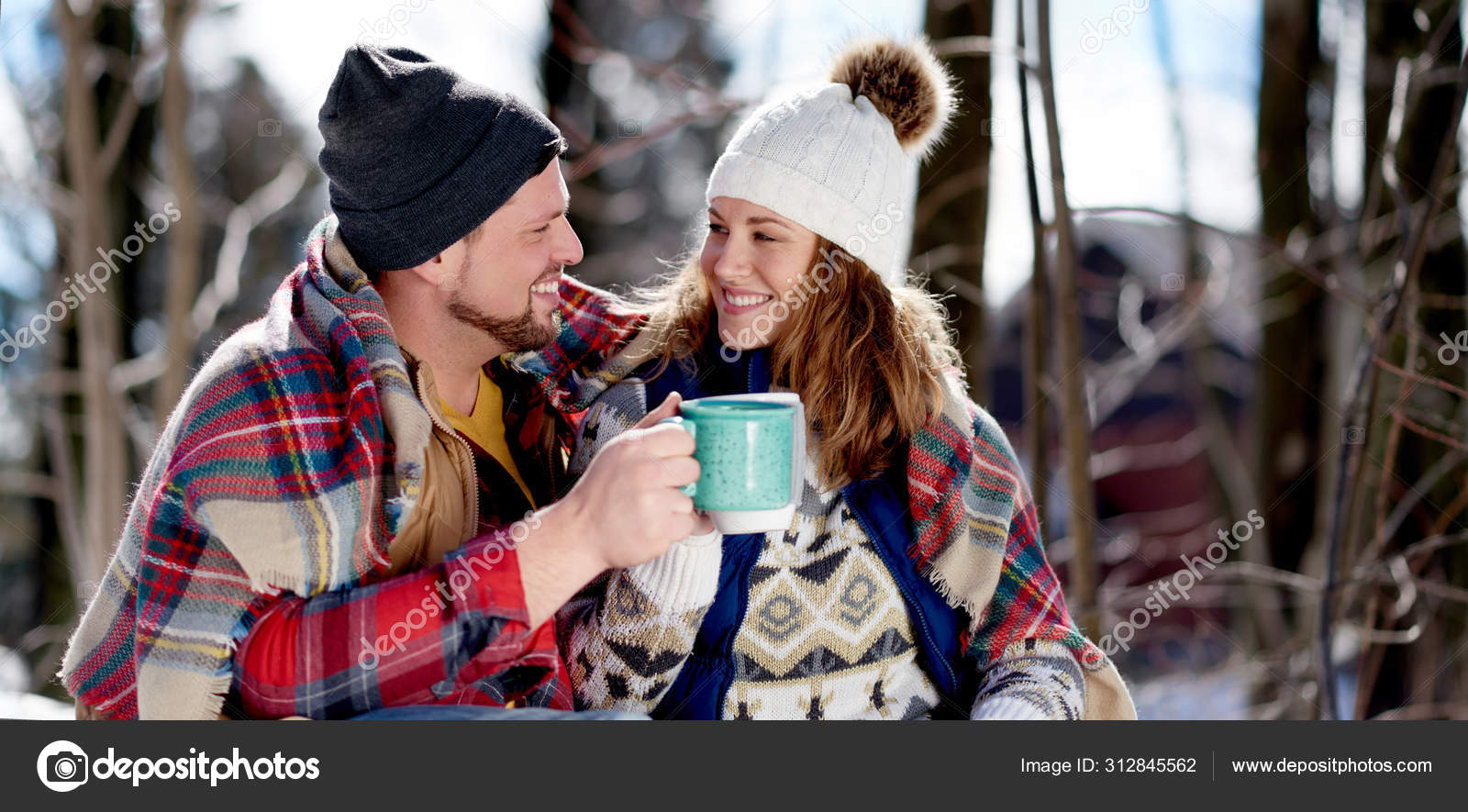 Couple in love enjoying a tender moment in fresh snow during wintertime and drinking hot ...