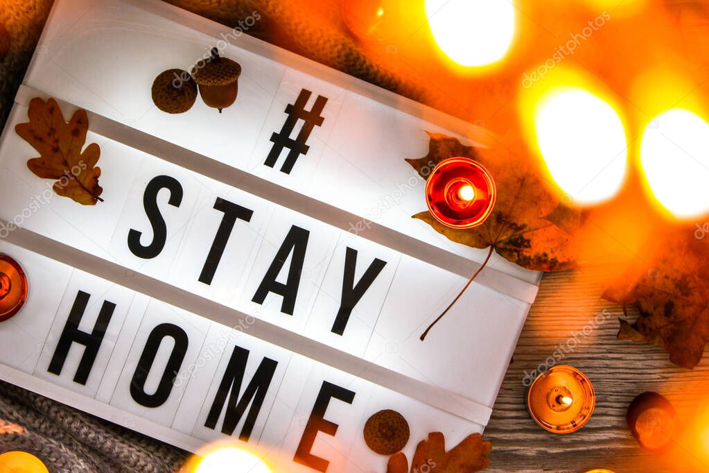 Hashtag Quédate en casa. Texto en caja de luz blanca, con un fondo de suéter, velas, hojas secas ...
