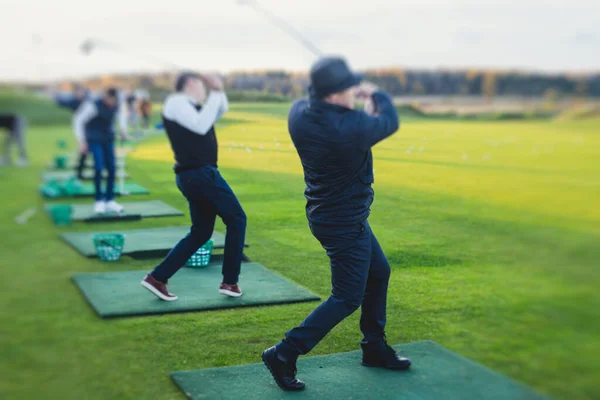 Group of golfers practicing and training golf swing on driving range ...