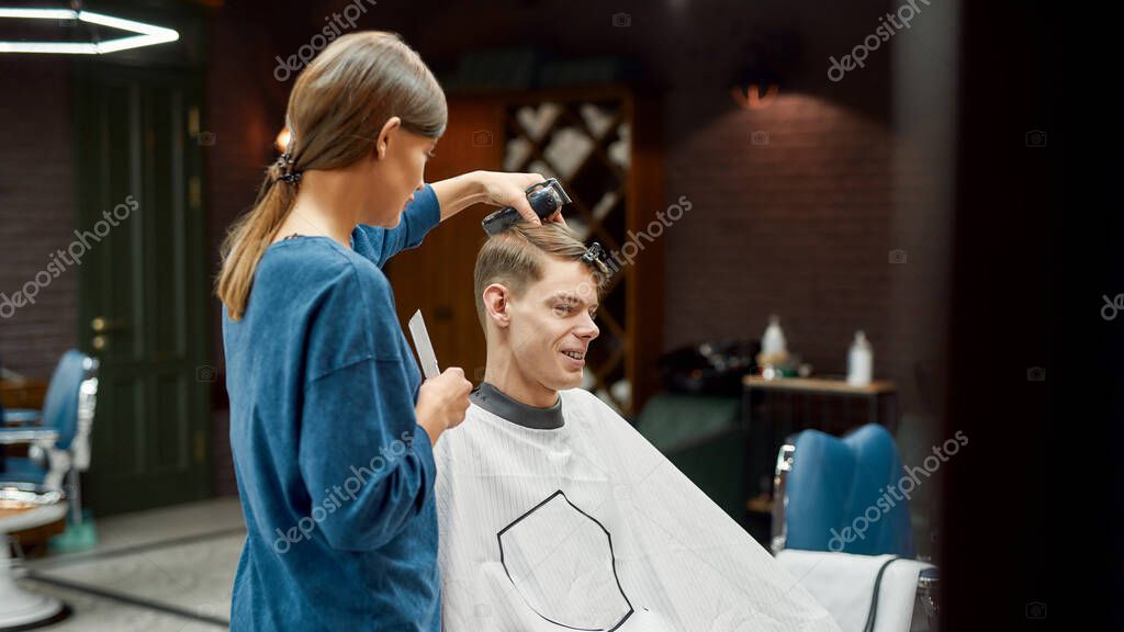 Peluquera profesional haciendo un nuevo corte de pelo de moda para el cliente, trabajando con la ...