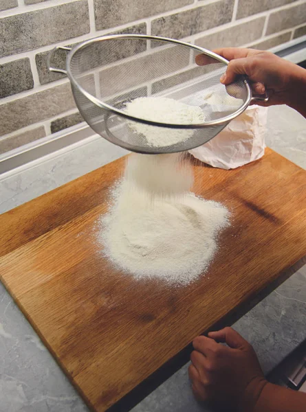 Cook hand sift flour through a sieve. Flour is strewed on a wooden ...