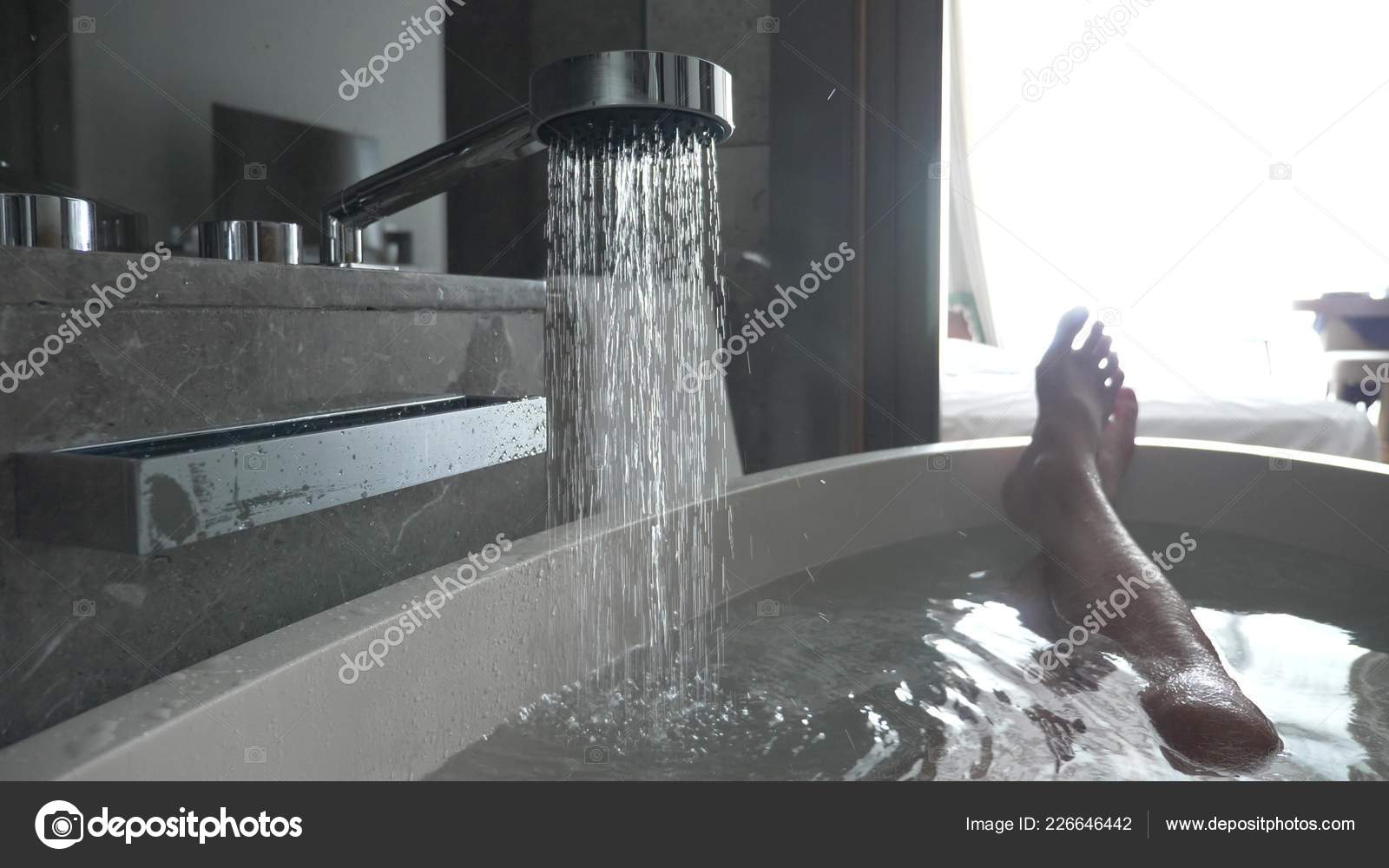 Mans legs in a bathroom of hotel. hot water pours into the bath and ...