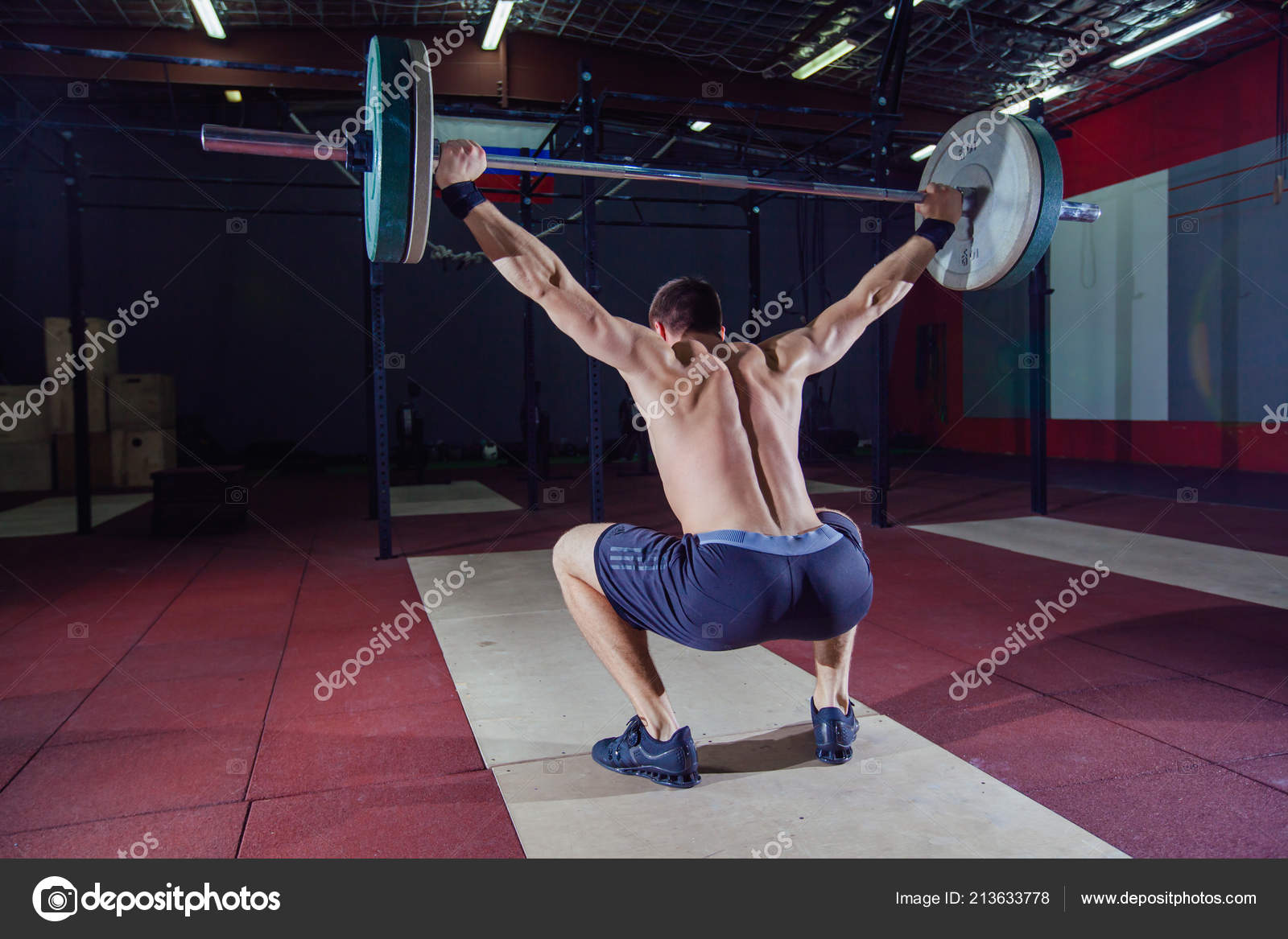Sporty man performing overhead squats with a heavy barbell at the gym ...