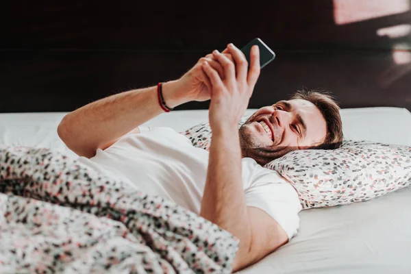 Young man using smartphone in bed in the morning - Stock Image - Everypixel