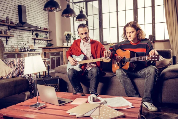 Young talented musicians playing the guitar sitting on sofa at home ...