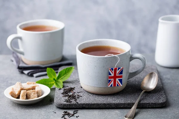 Tea in mugs with British flag tea bag label. Grey background. Close up ...