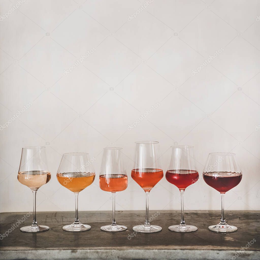Varios tonos de vino rosa en copas de tallo colocadas en línea de color ...