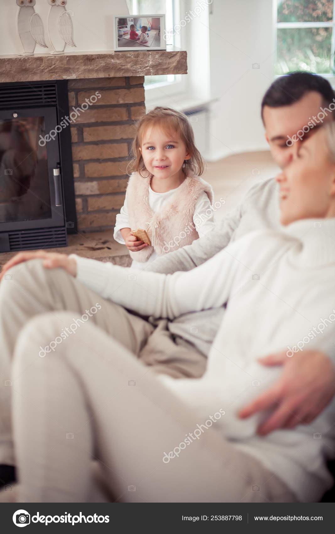 The family sits on the couch near the fireplace. Mom, Dad, daughter in the home interior. Cozy ...