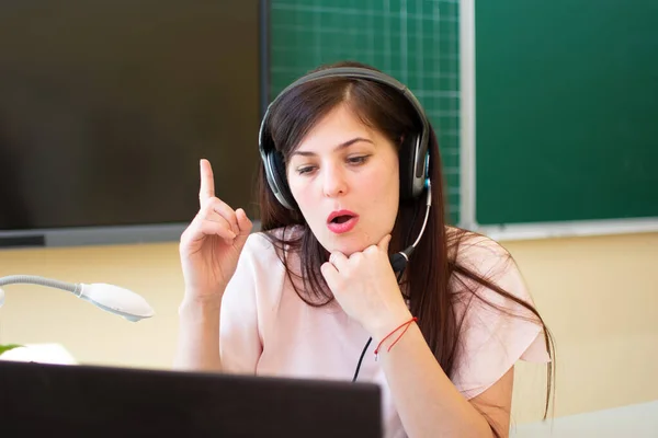 Young female teacher headphones with microphone conducts online lessons ...