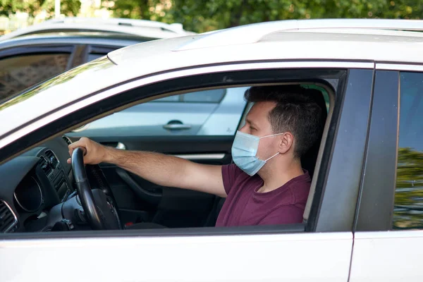 A man driving a car in a medical face mask during coronavirus outbreak ...