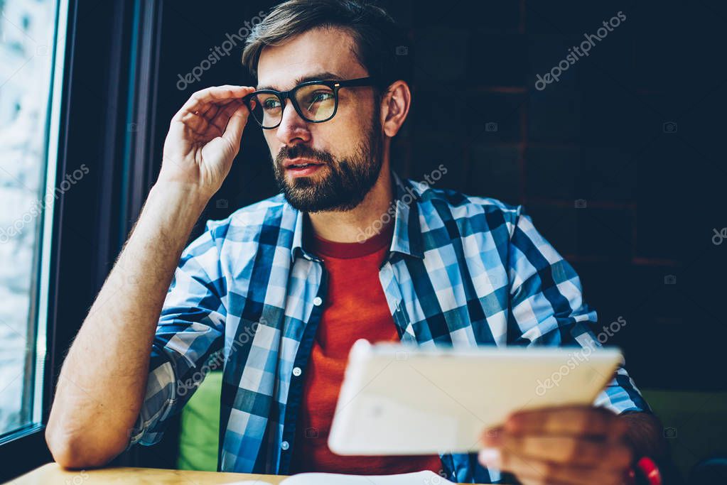 Joven barbudo reflexivo con almohadilla táctil mirando hacia otro lado ...