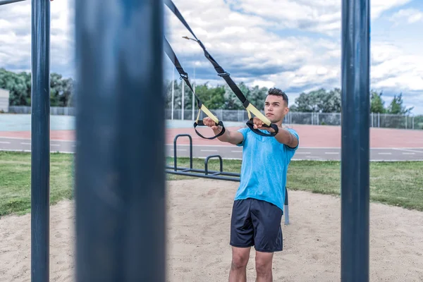 Handsome and muscular athlete man, close-up, training on loops, webbing ...