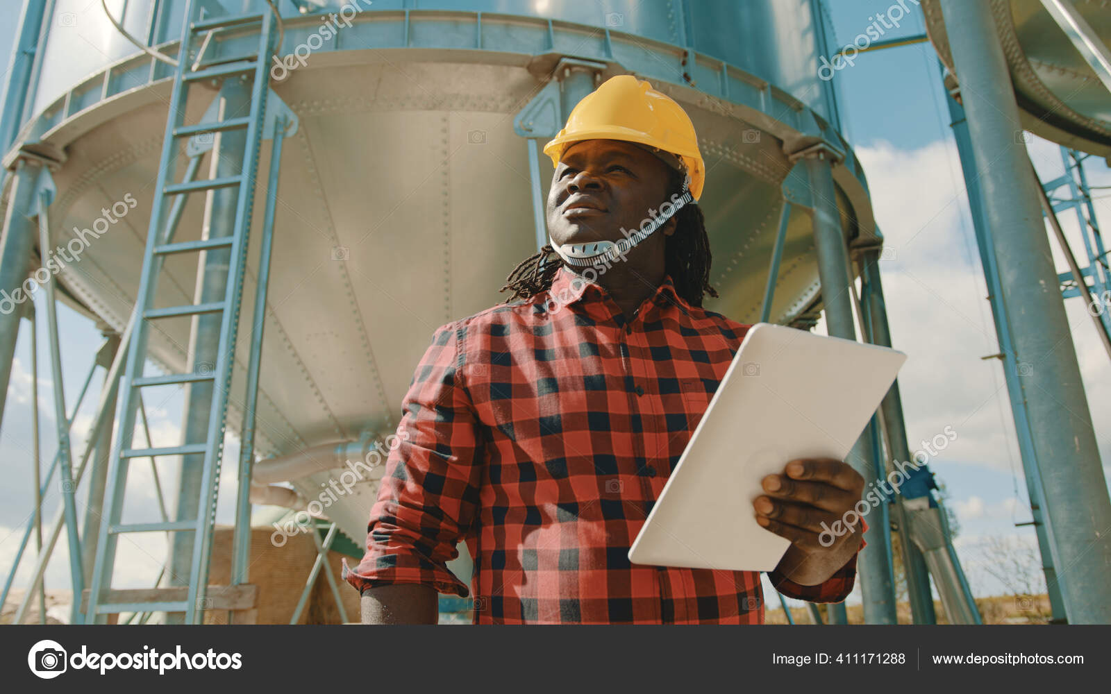 Young handsome african man, engineer with safety helmet using tablet in ...