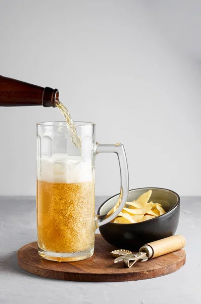 Lager beer pouring in glass and bottle with potato chips on gray ...